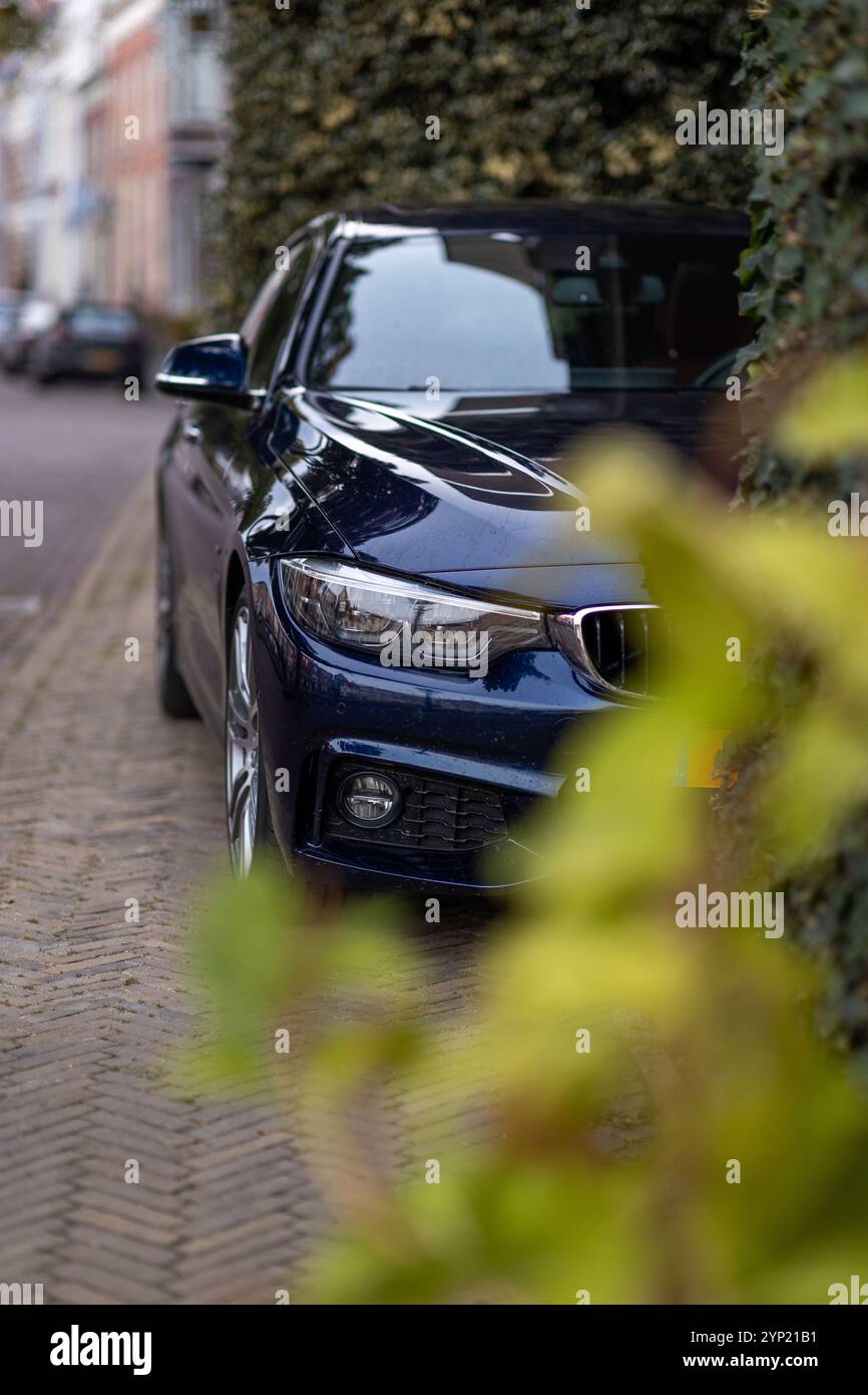 A sleek dark blue car parked on a cobblestone street, partially hidden ...