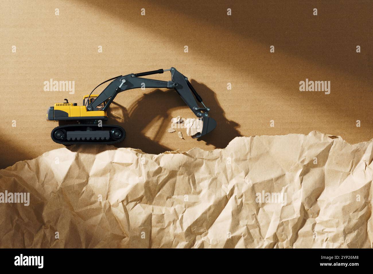 Small toy excavator digging soil, cardboard and paper background ...