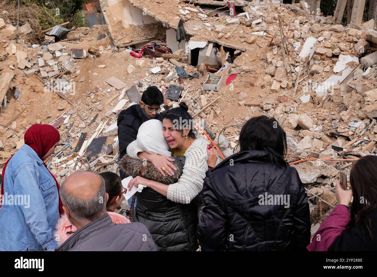 Displaced residents hug as they stand in front of the rubble of their ...
