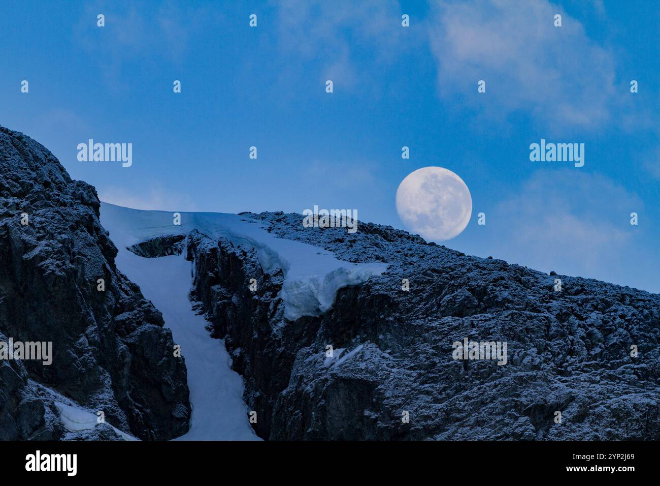 View of the nearly full moon rising over snow-covered mountains on the ...