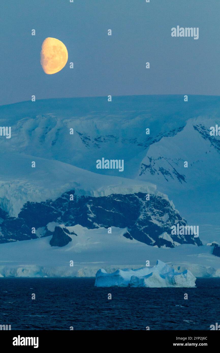 View of the nearly full moon rising over snow-covered mountains on the ...