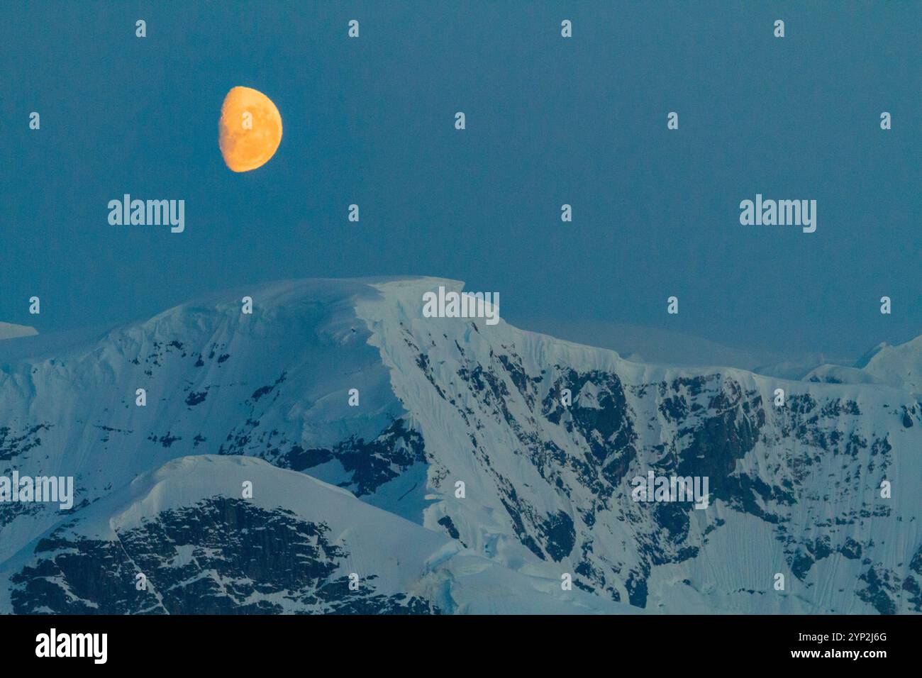 View of the nearly full moon rising over snow-covered mountains on the ...