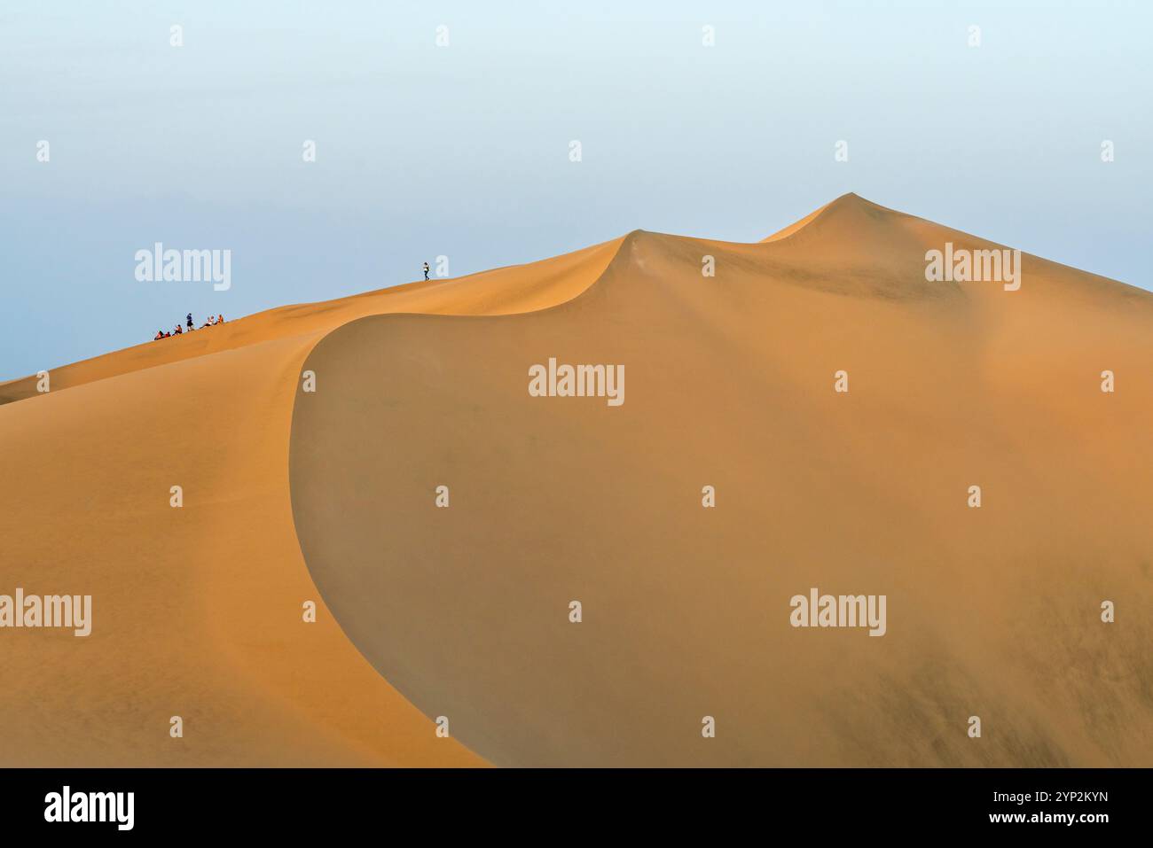 Distant view of tourists watching sunset from sand dune in desert ...