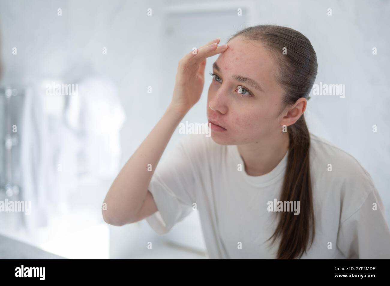 Gen z woman looking at her acne on forehead, stands before a mirror in ...