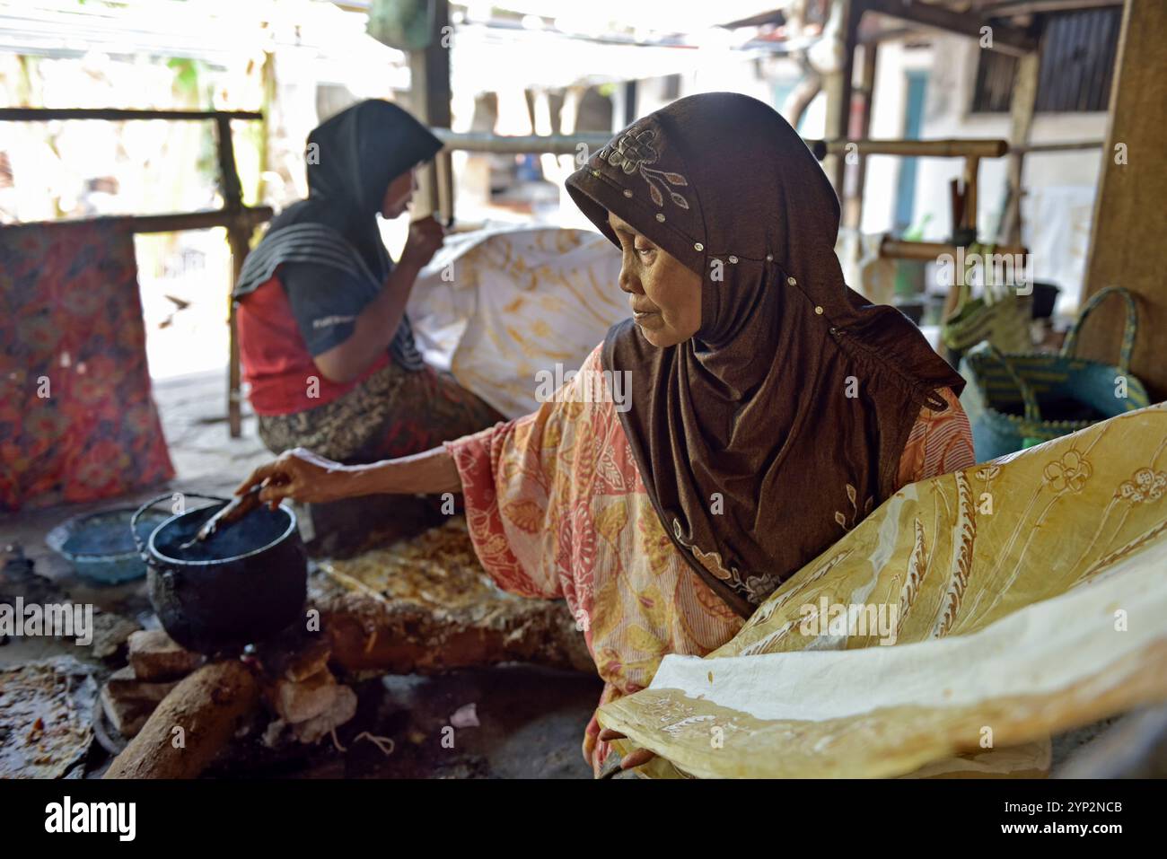 Women using a pen-like tool (canting) to apply liquid hot wax to create pattern on the fabric ...