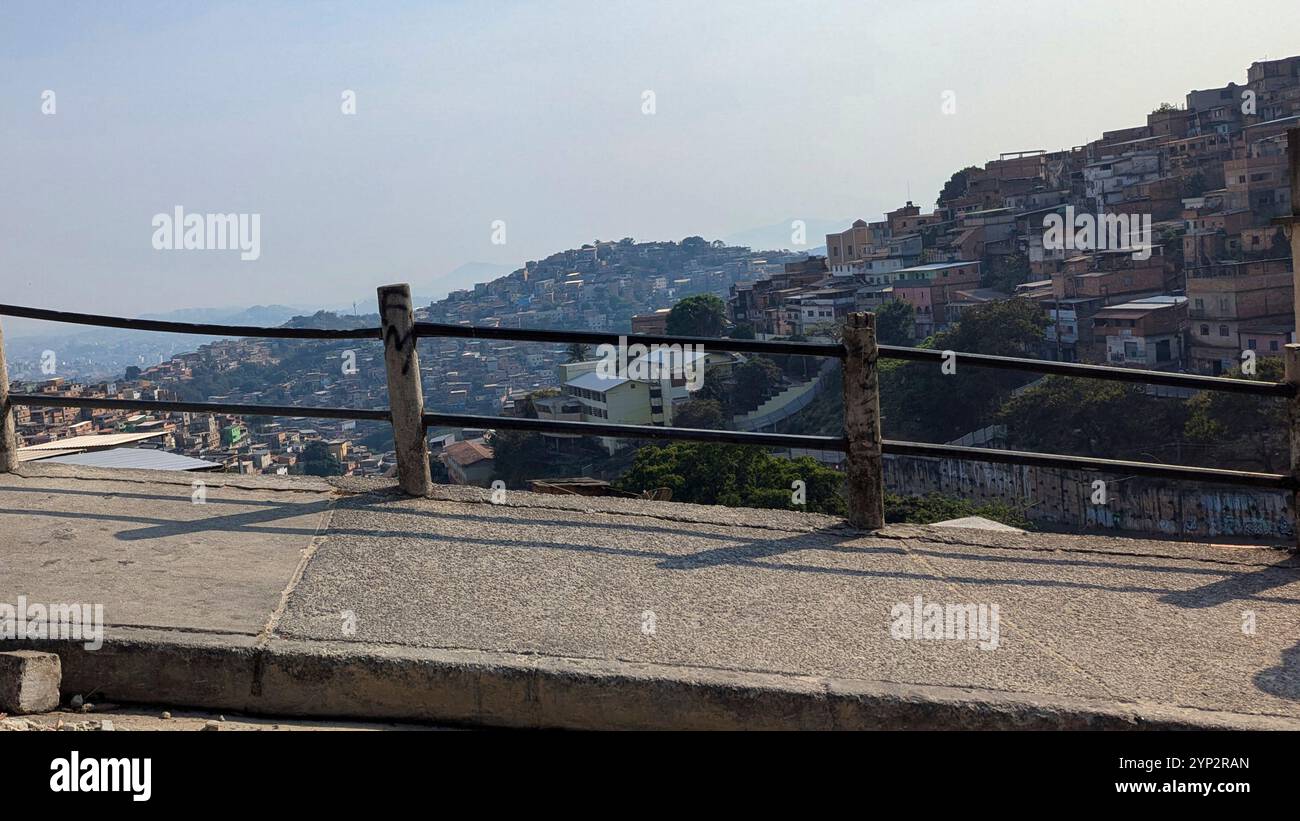 A fence is on the side of a road with a view of a slum. The fence is ...