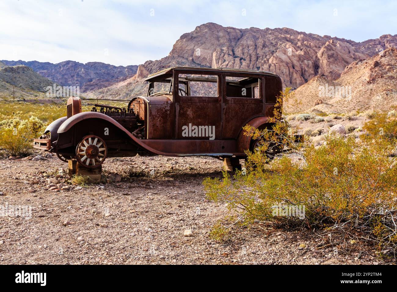 An old car is sitting in the desert. The car is rusted and has a lot of ...