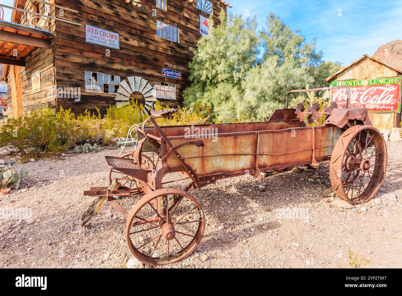 An old, rusted farm wagon sits in front of a building with a Coca-Cola ...