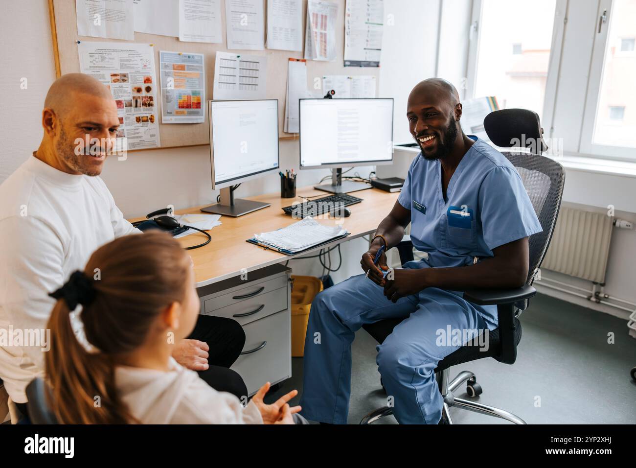 Happy doctor talking with girl sitting next to father in medical ...