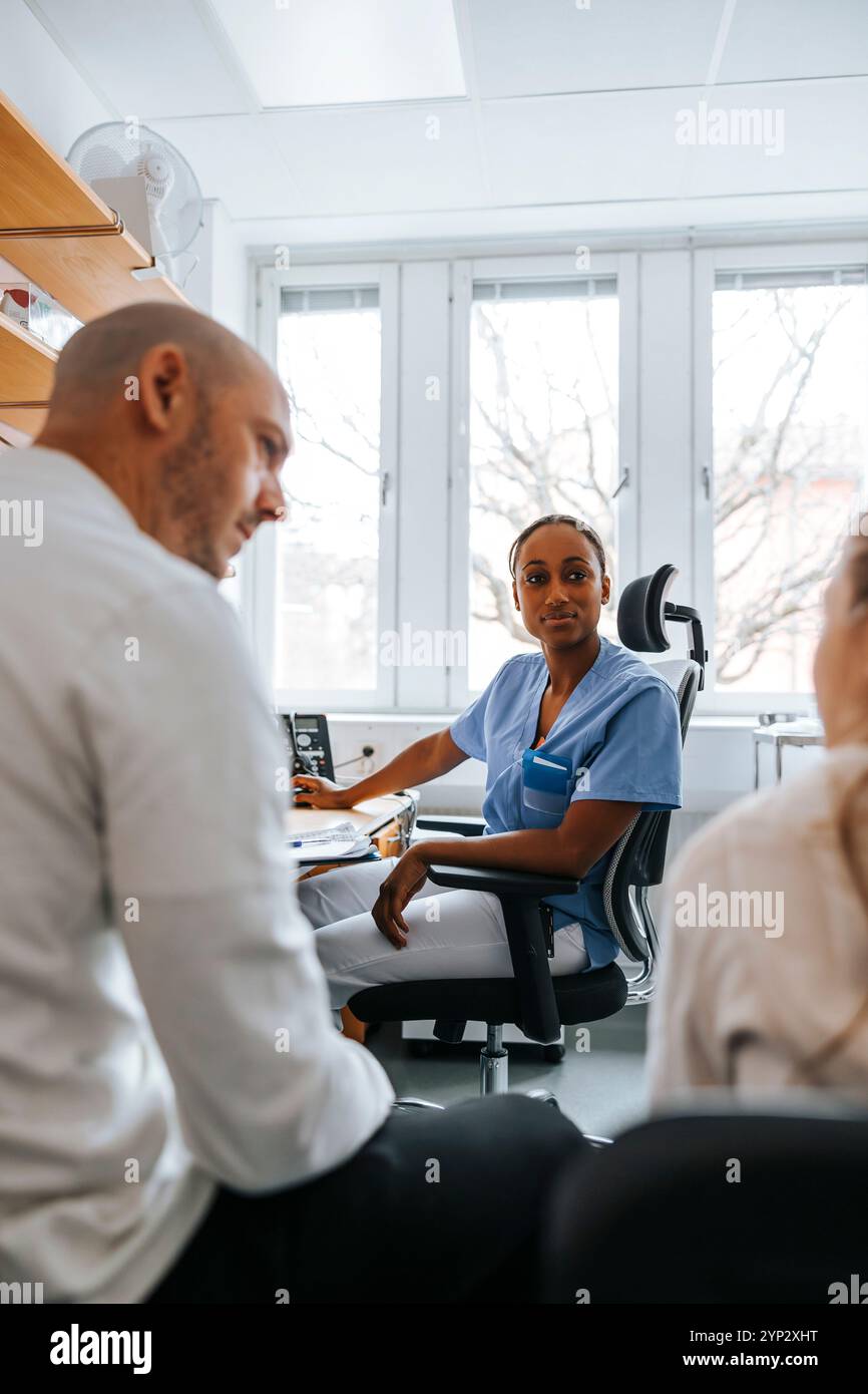 Female medical professional sitting on chair with patients in ...