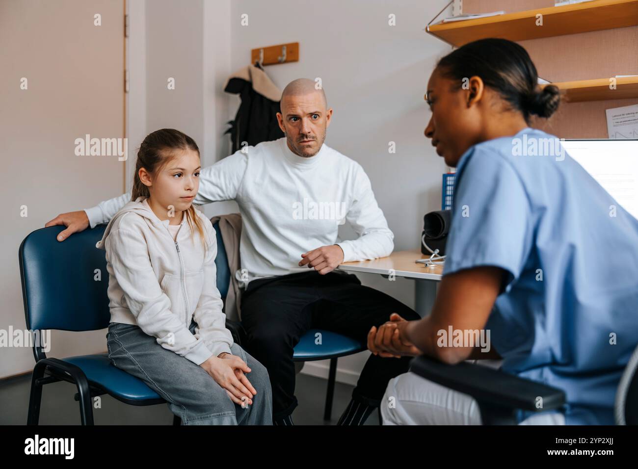 Serious father and daughter sitting and discussing with female doctor ...