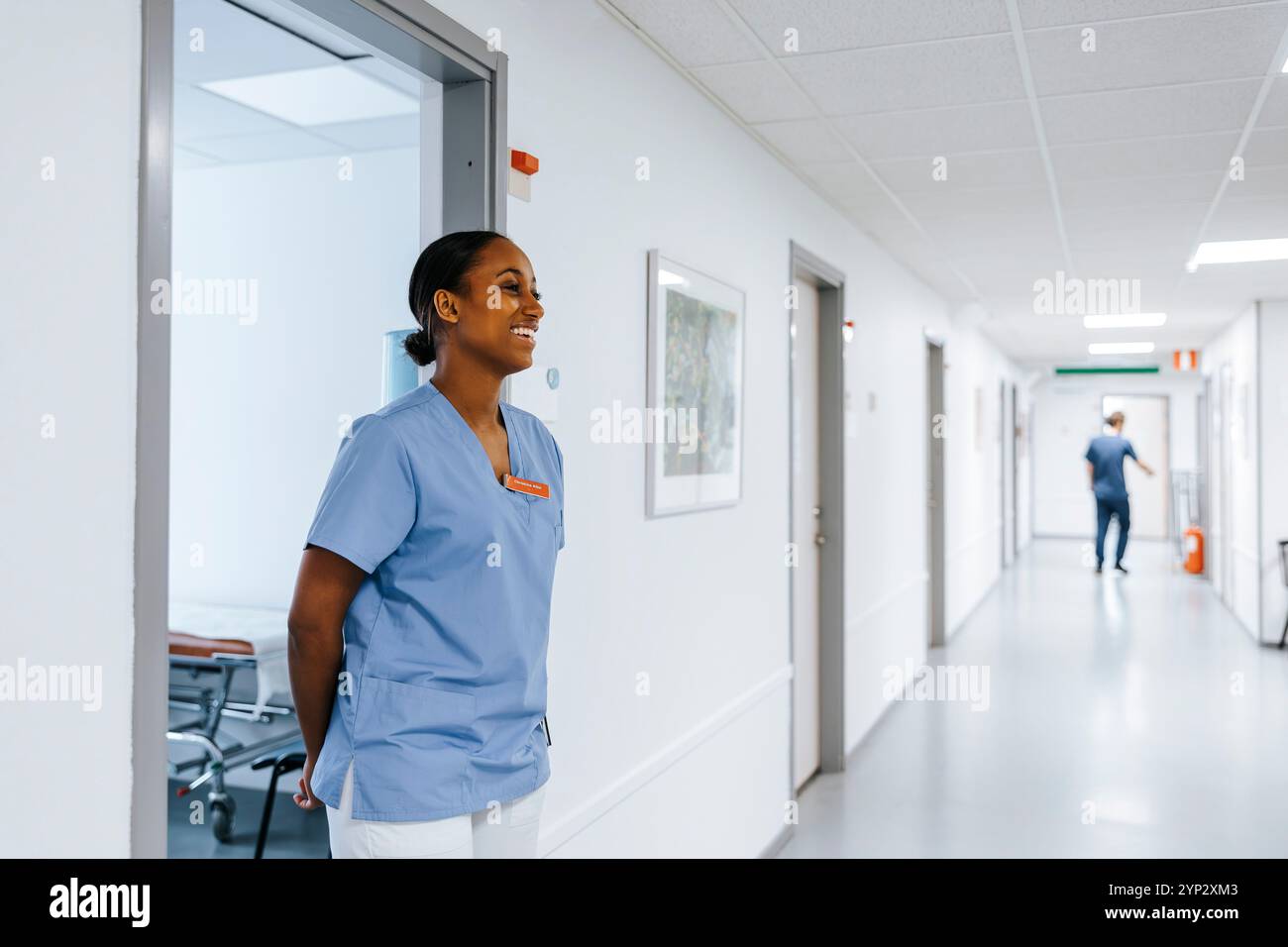 Happy female doctor with hands behind back standing on doorway of ...
