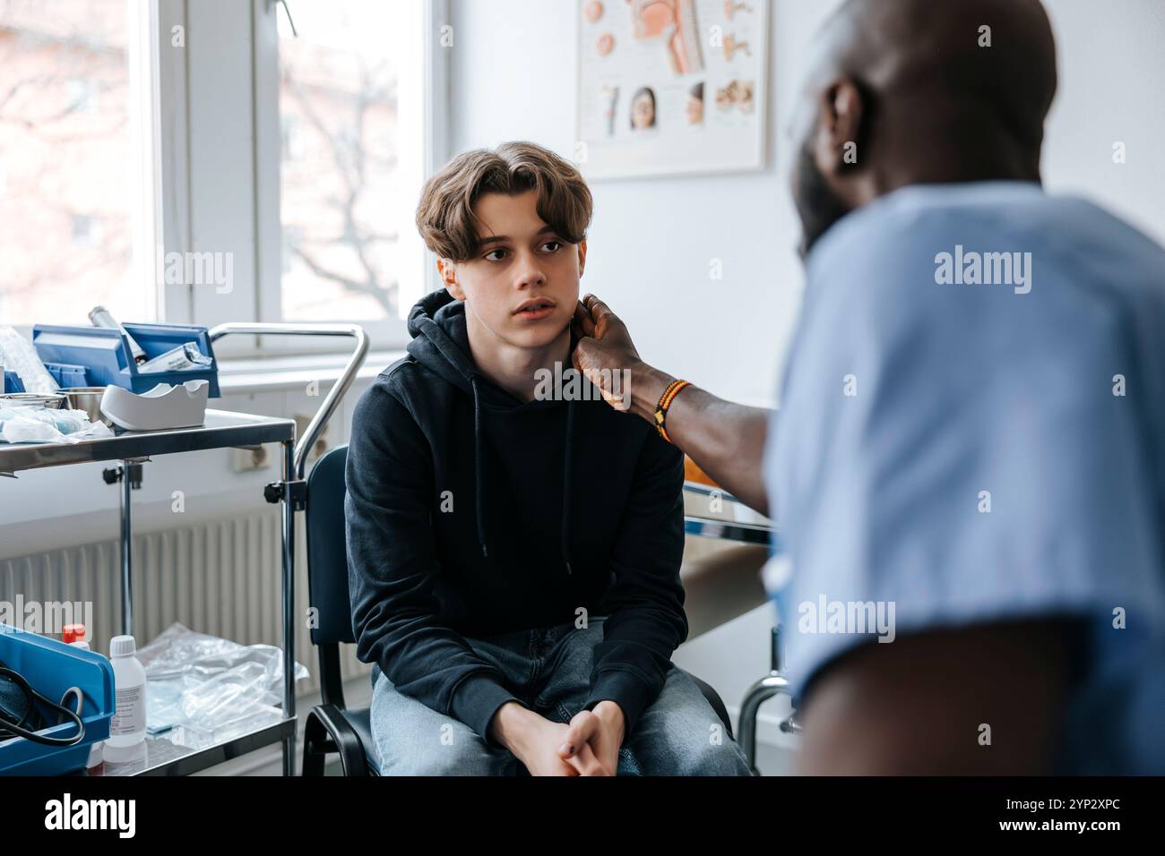 Male doctor checking neck of teenage patient while sitting in medical ...