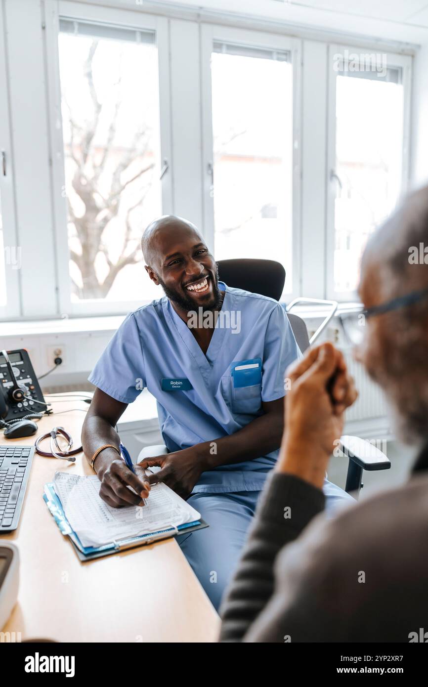Happy male medical expert talking with patient while sitting near table ...