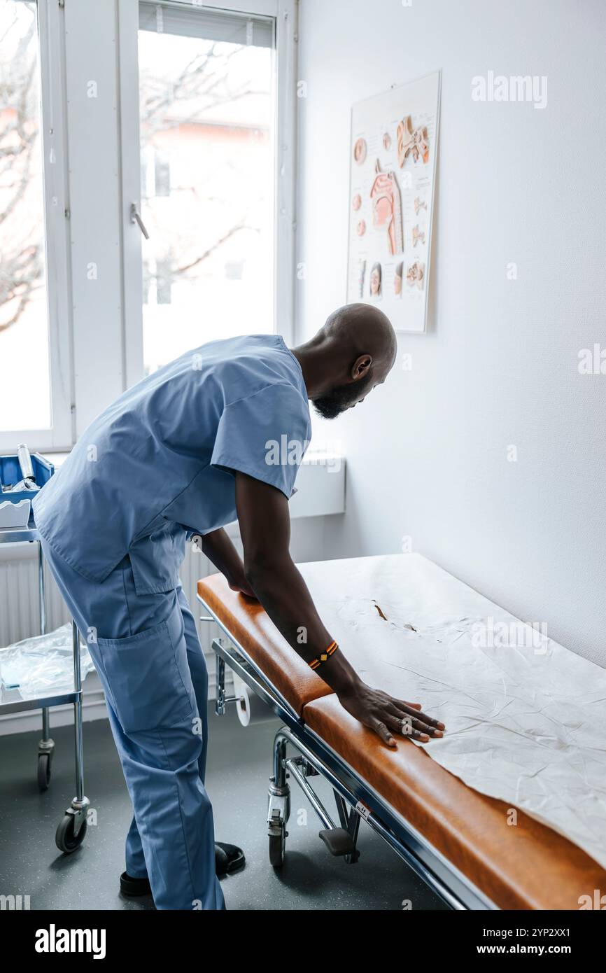 Side view of male healthcare worker putting sheet on bed in medical ...