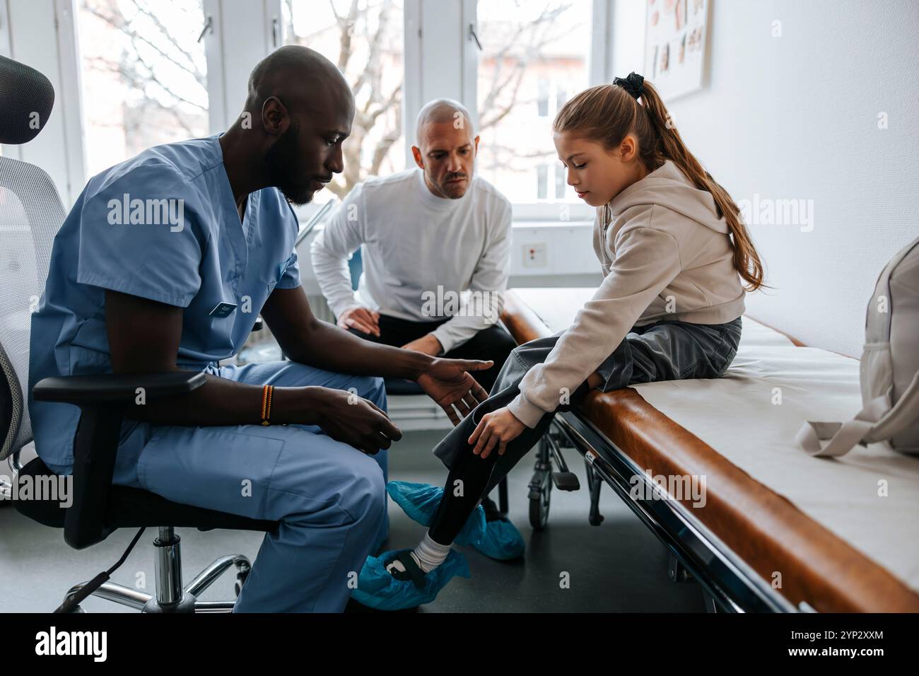 Side view of male doctor checking leg of girl sitting on bed with ...