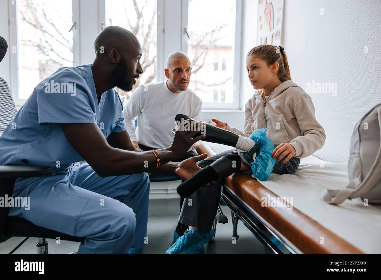 Side view of male doctor checking artificial limb of girl sitting on ...