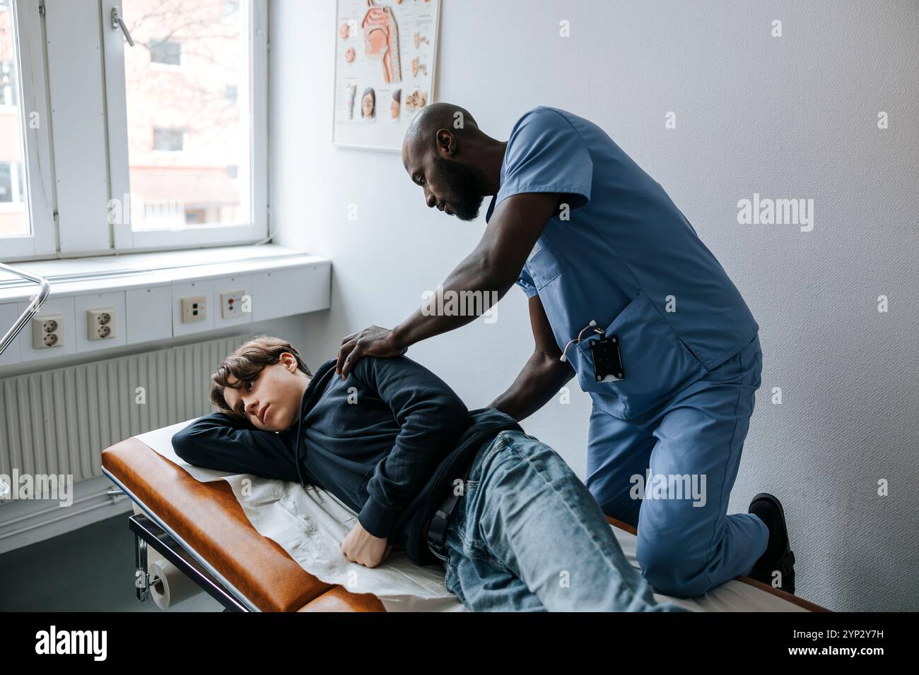Male medical professional checking back of teenage boy lying on bed in ...