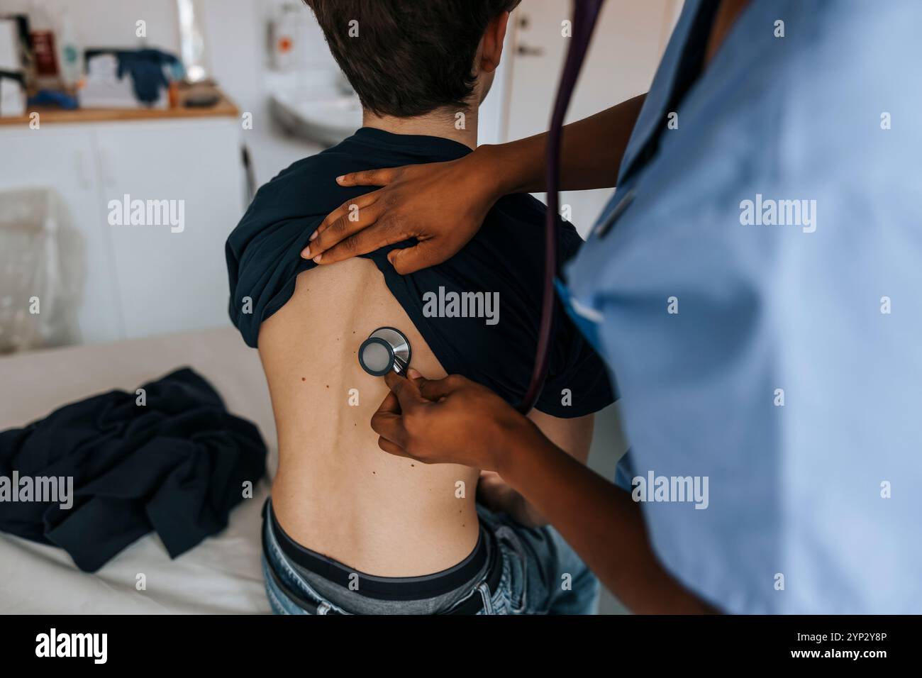 Female healthcare worker examining boy's back with stethoscope in ...