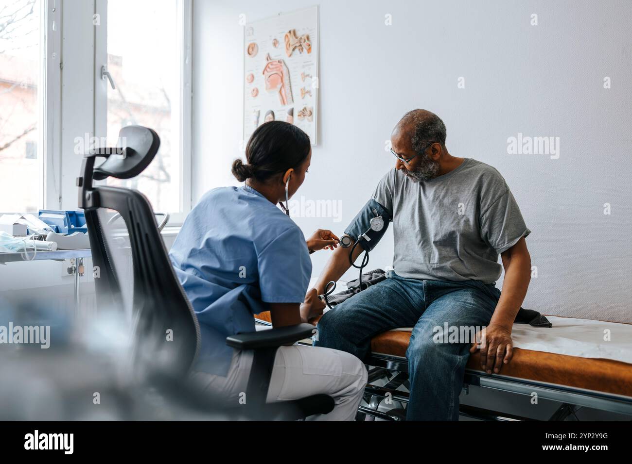 Female doctor checking senior patient's blood pressure sitting on bed ...