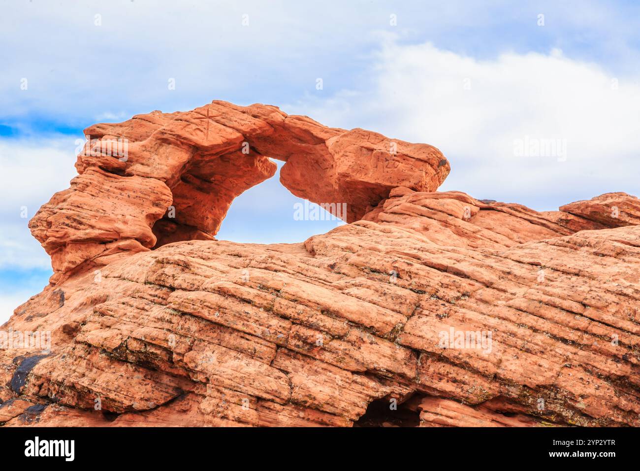 A large rock formation with a small hole in the middle. The rock is red ...