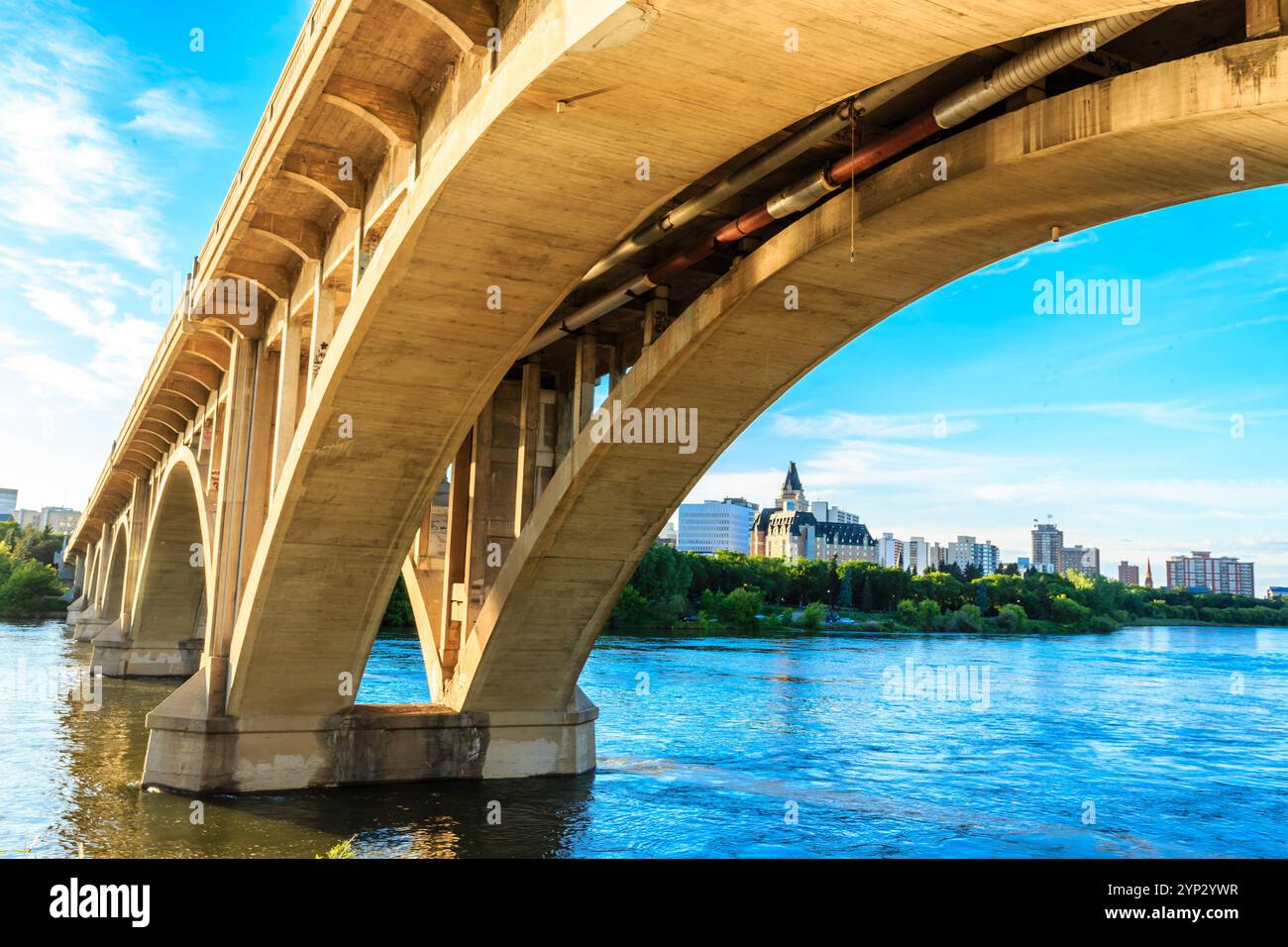 A bridge spans a river with a city in the background. The bridge is a ...