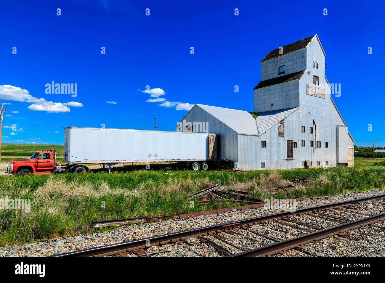 A red truck is parked in front of a large grain silo. The silo is ...