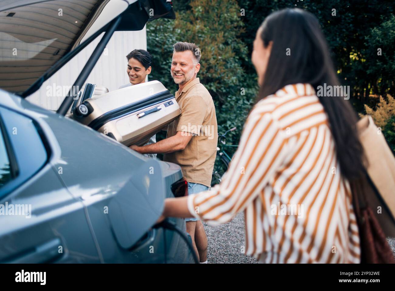 Rear view of woman charging car while happy man loading luggage with ...