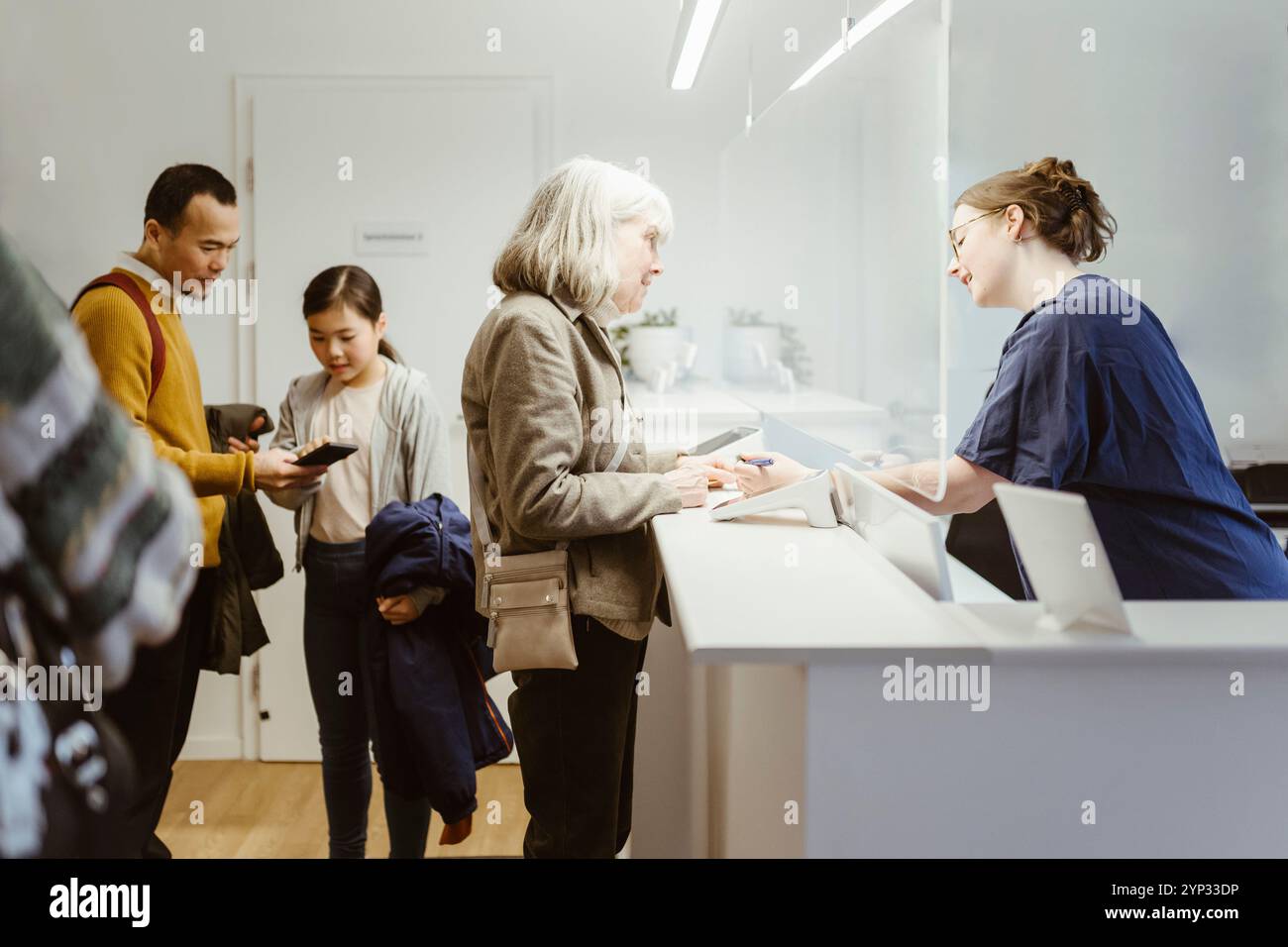 Female medical staff assisting senior woman in filling form during ...