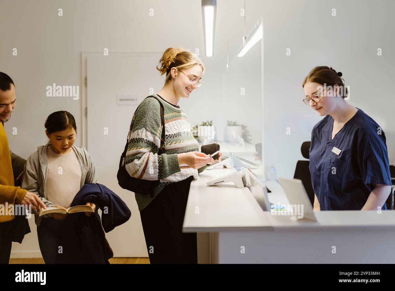 Smiling young woman booking doctor's appointment while standing at ...
