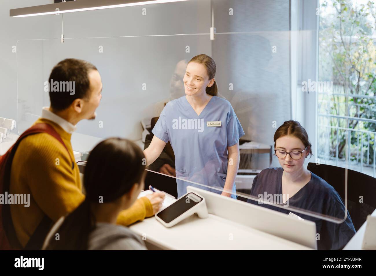 Smiling female receptionist interacting with patient through glass ...