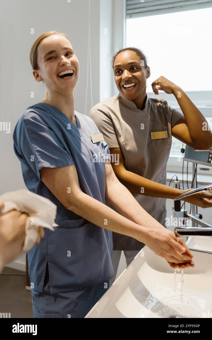 Happy female nurse laughing while washing hands in sink at hospital ...