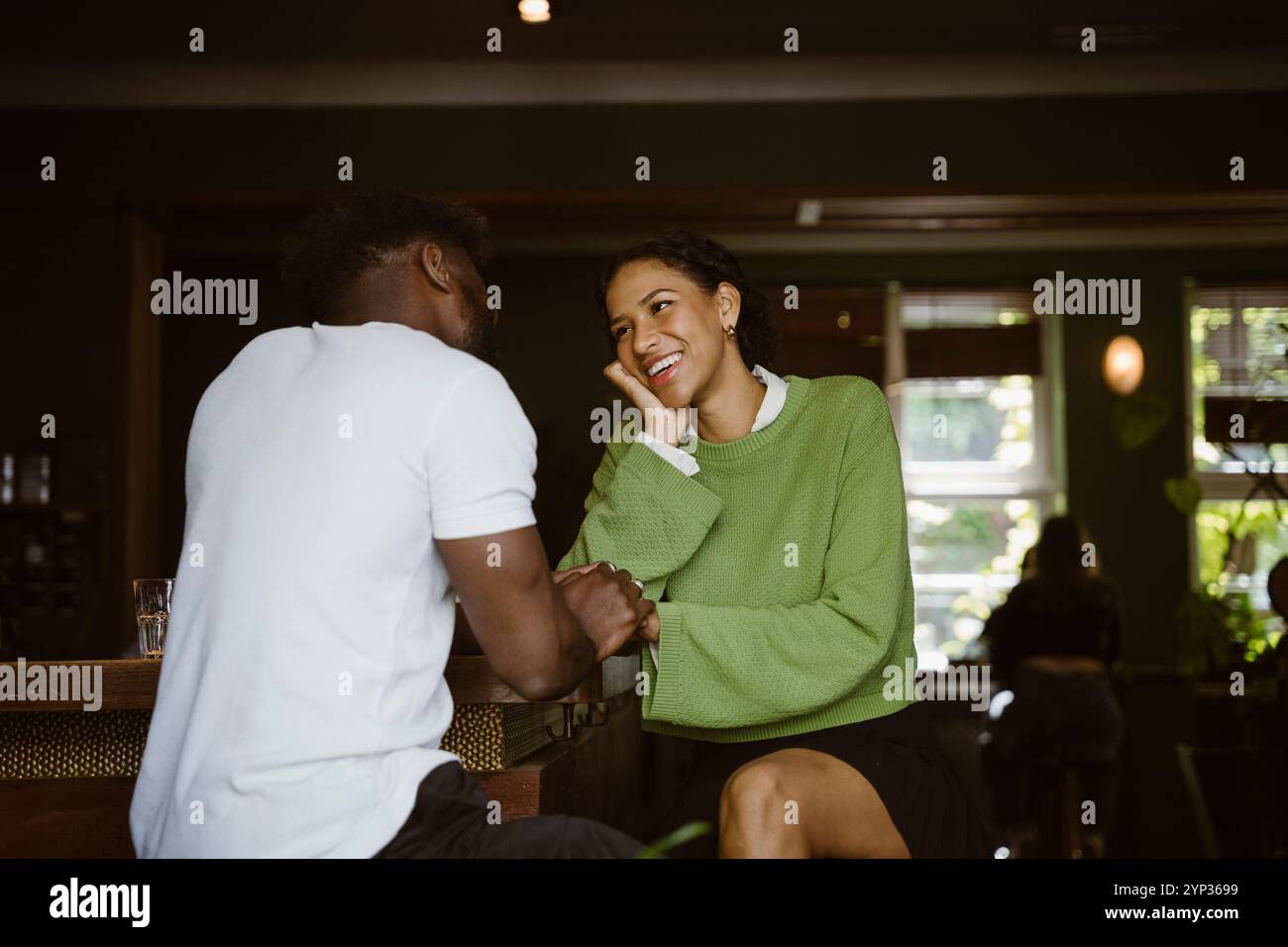 Smiling woman leaning on elbow and glancing at boyfriend sitting in bar ...