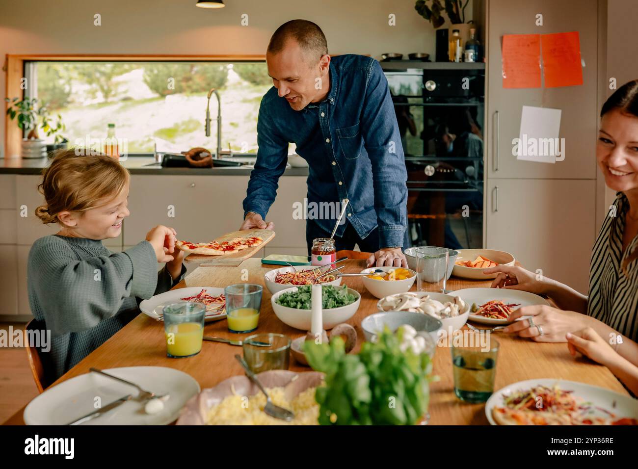 Father giving pizza to son sitting near dining table for lunch at home ...