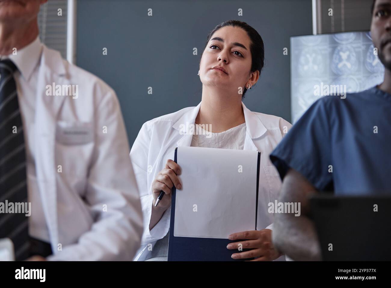 Medium shot of thoughtful Middle Eastern female physician attending lecture at conference room ...