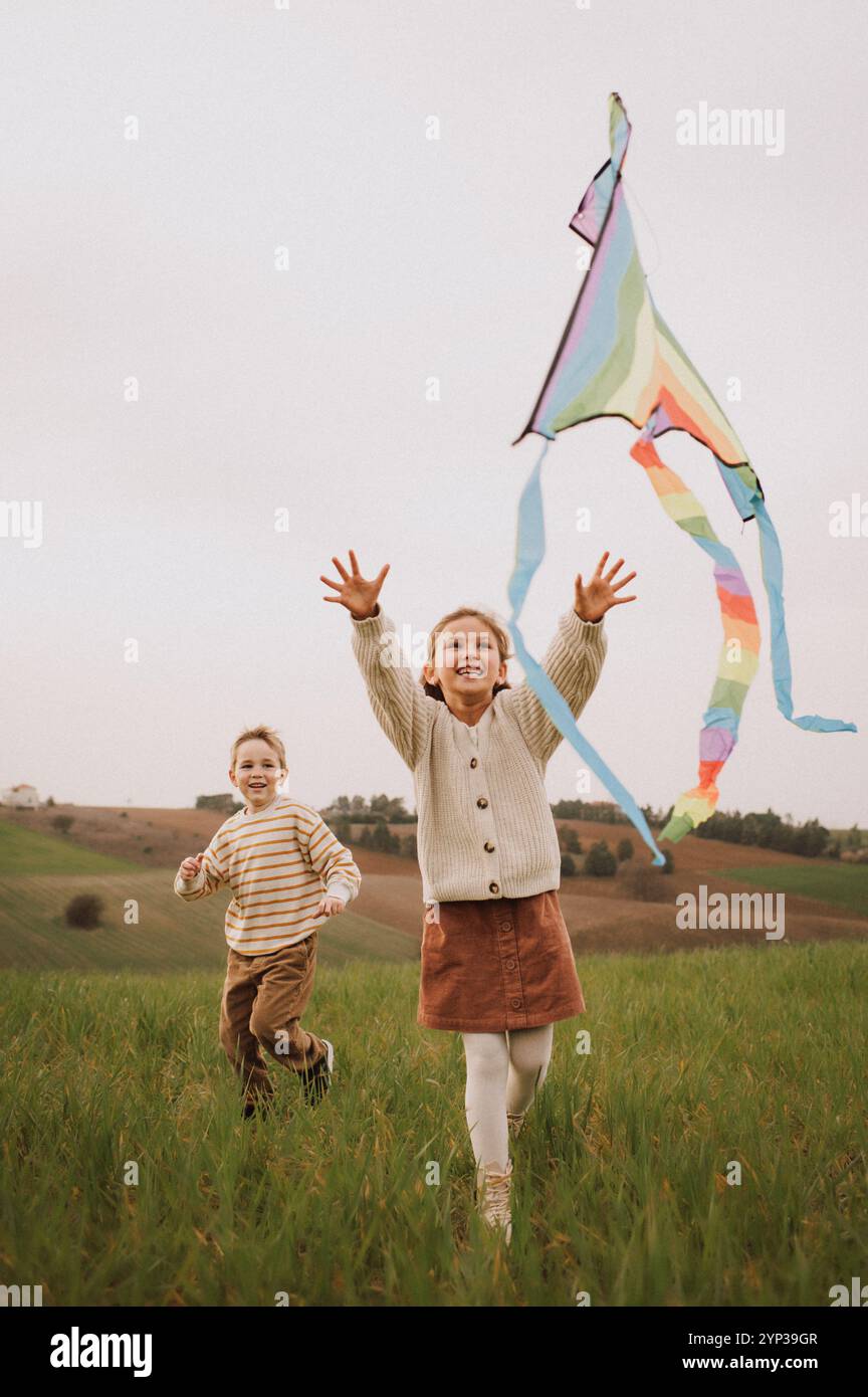 two kids are running in a field trying to catch kite Stock Photo - Alamy