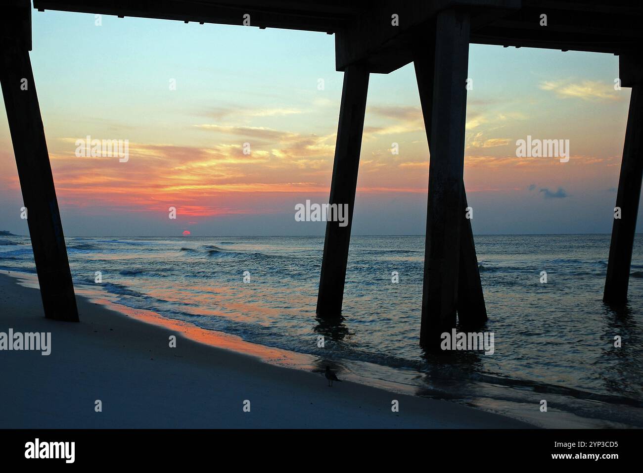 The wood support beams and pylons of a pier frame the sunrise over the ...