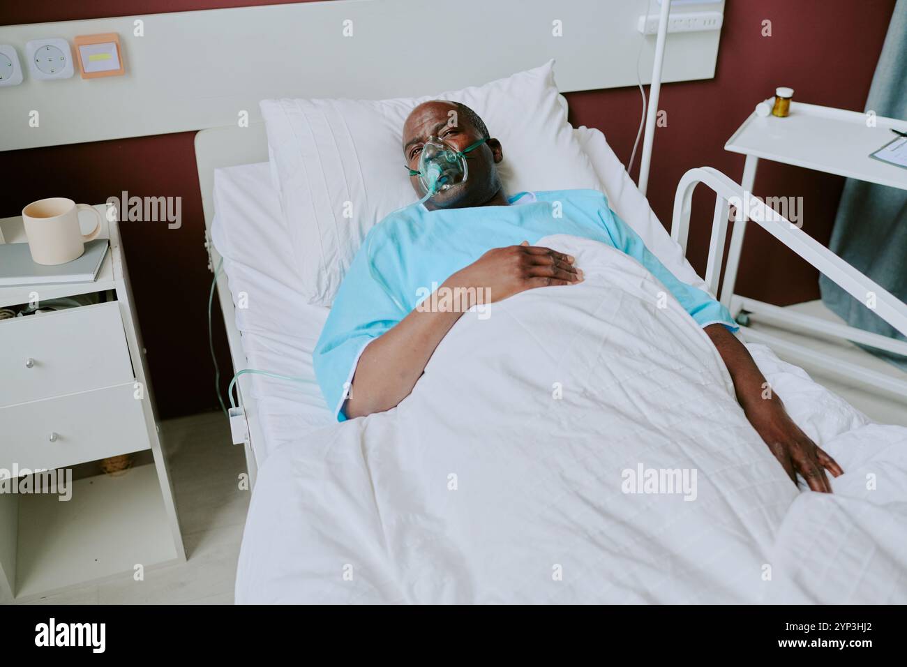 African American patient lying in hospital bed wearing oxygen mask and blue gown, situated in a ...
