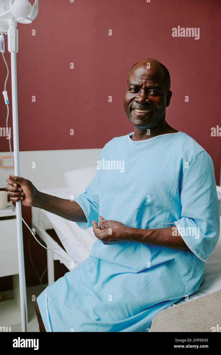 Smiling African American patient sitting on hospital bed, holding IV ...