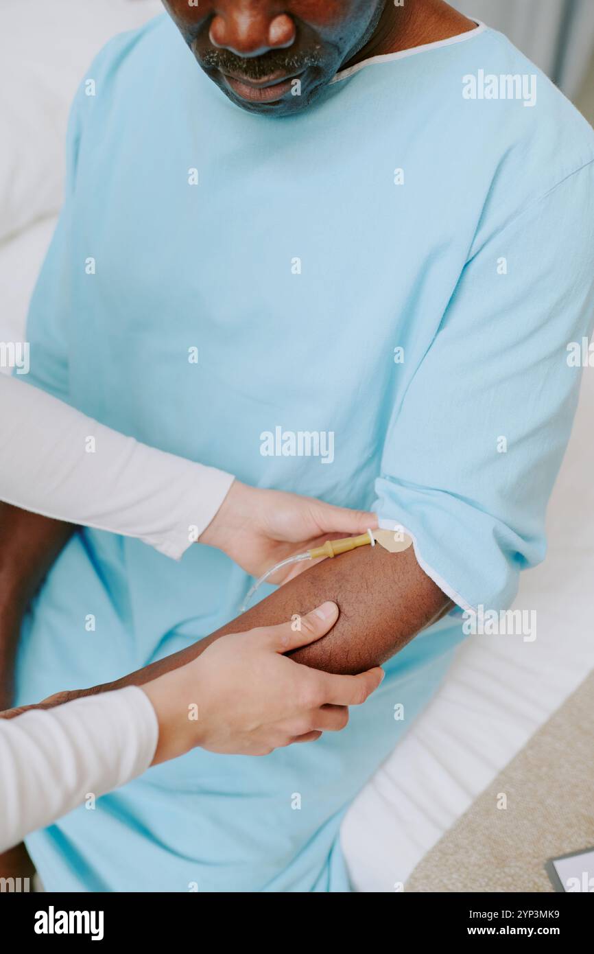 Nurse inserting IV into arm of patient sitting in a hospital bed ...