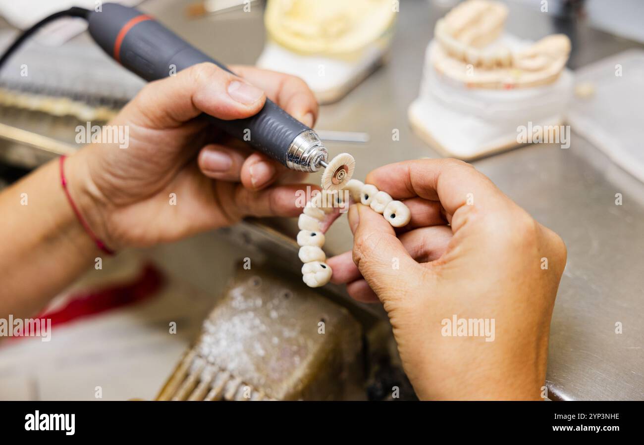 A dental technician carefully polishing a set of prosthetic teeth with ...