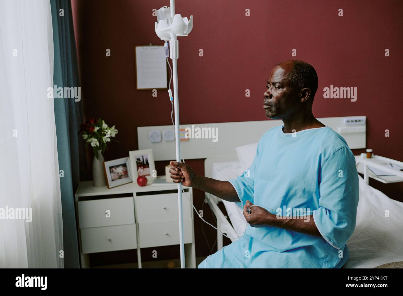 African American man sitting on hospital bed, holding IV drip and ...