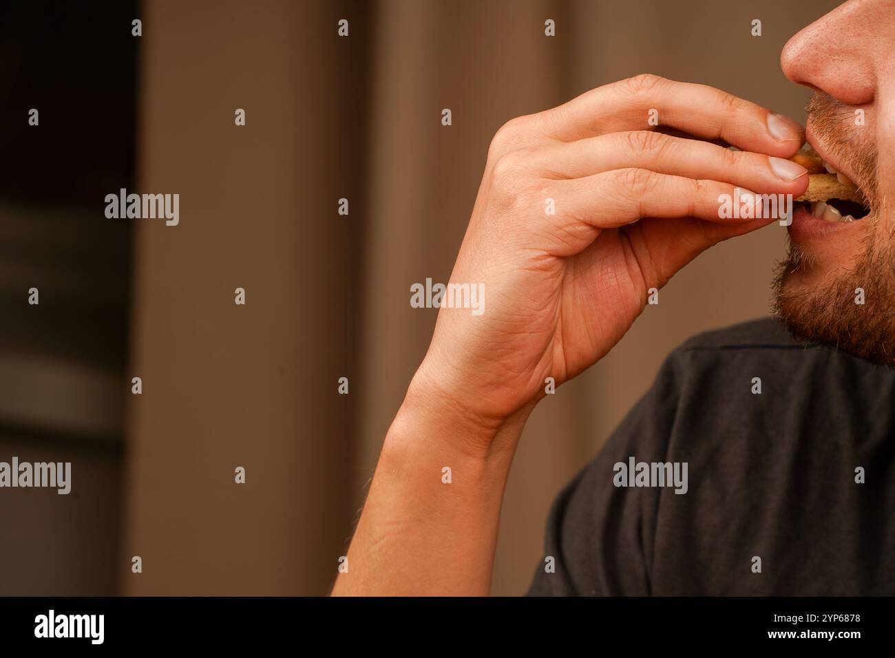 Close-up of a man eating a crispy bread snack while holding it in his ...