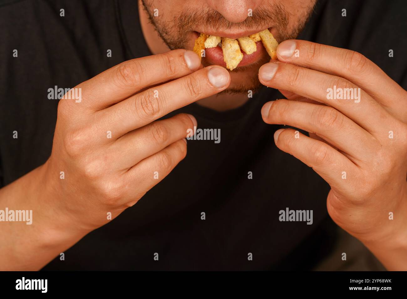 A man holds a small crunchy snack to his mouth, ready to eat. A close ...