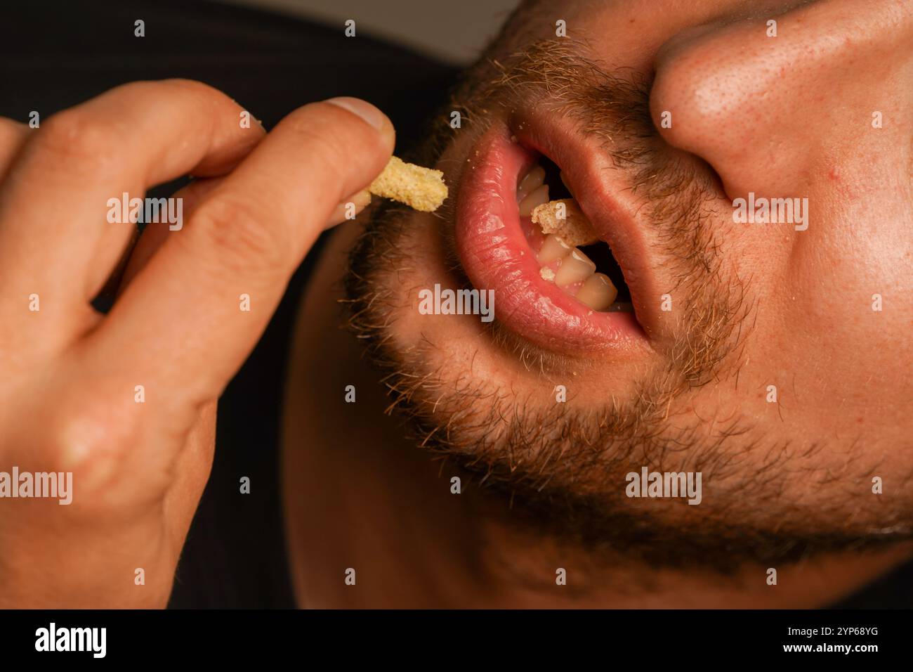 A close-up of a man about to eat a crunchy snack in the form of a ...