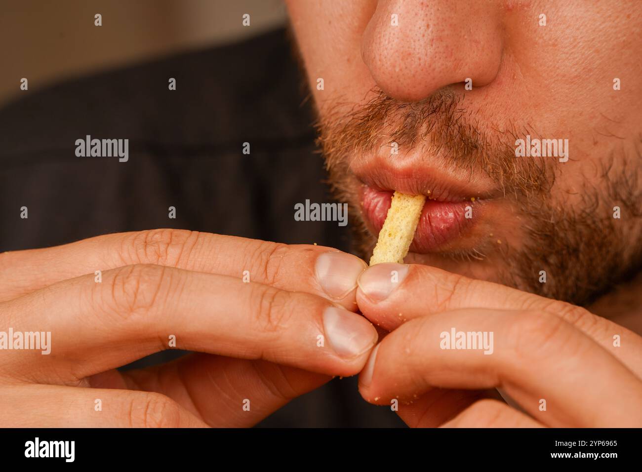 A close-up of a man about to eat a crunchy snack in the form of a ...