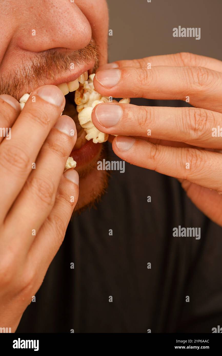 A close-up of a person eating popcorn with their hands, pouring it into ...