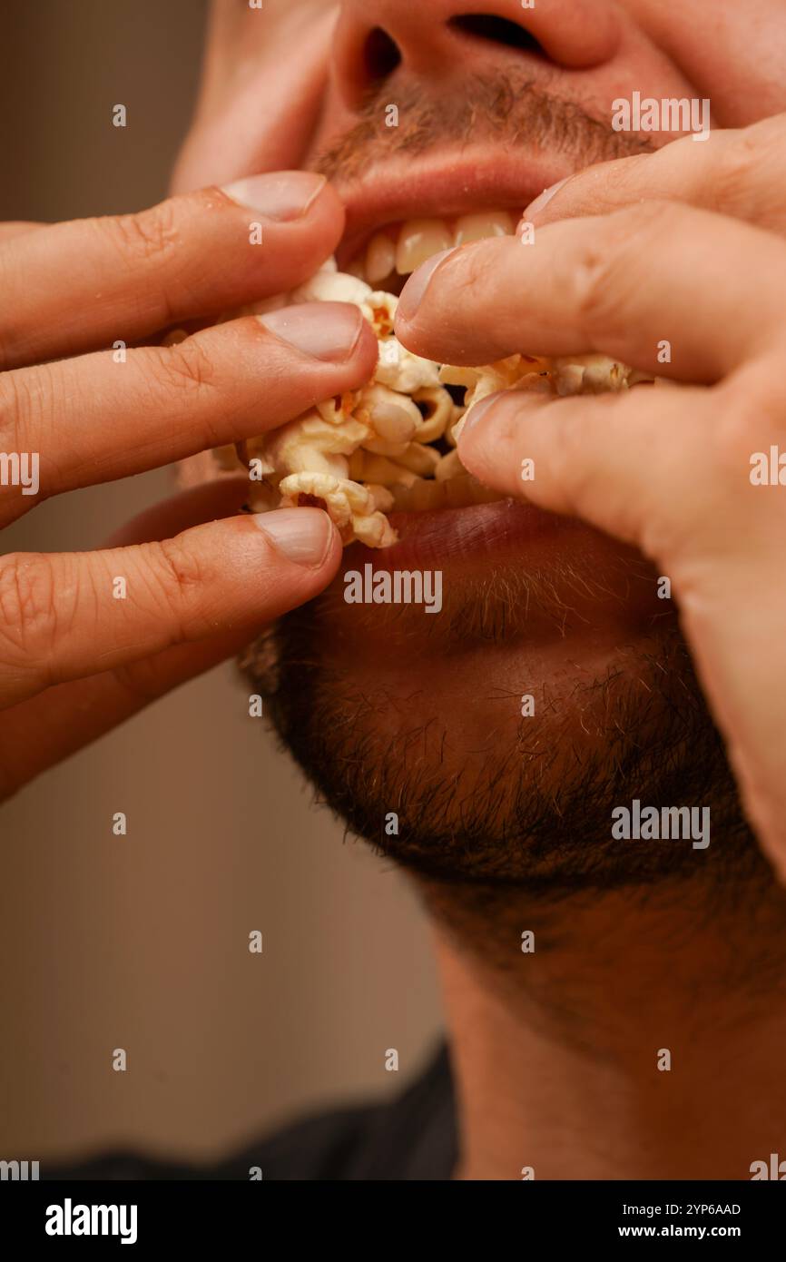 A close-up of a person eating popcorn with their hands, pouring it into ...