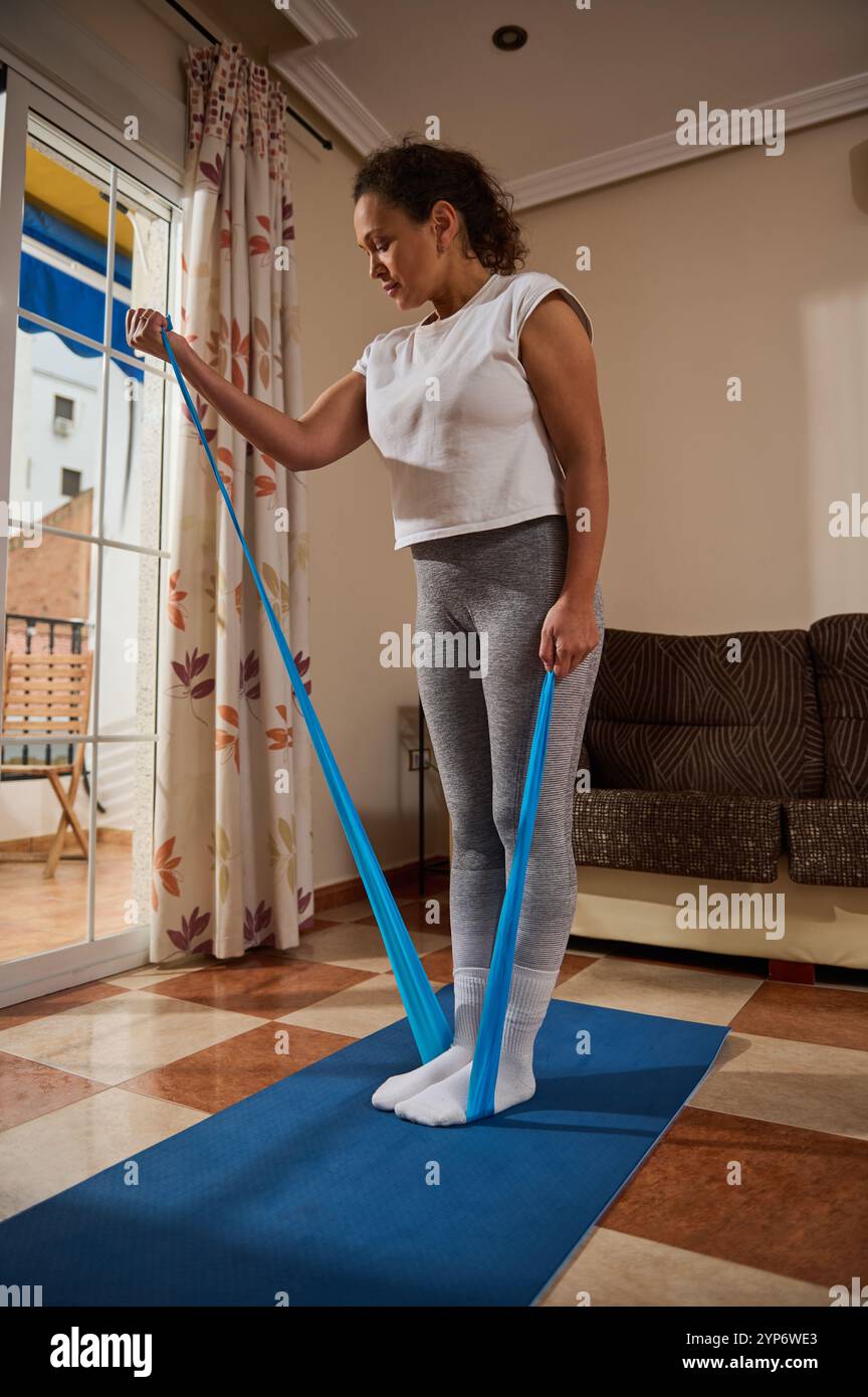 A woman practices strength training using a resistance band in her cozy ...