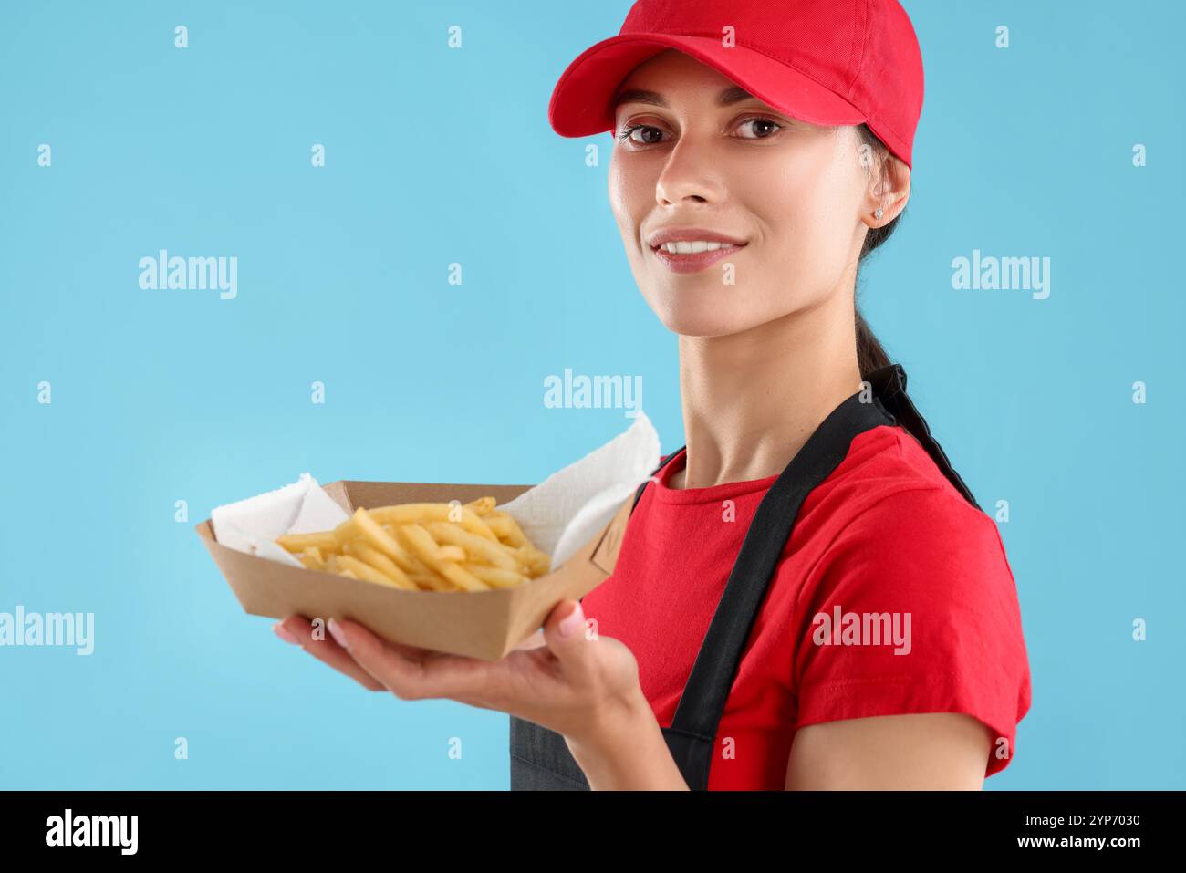 Fast-food worker holding paper container with fries on light blue ...